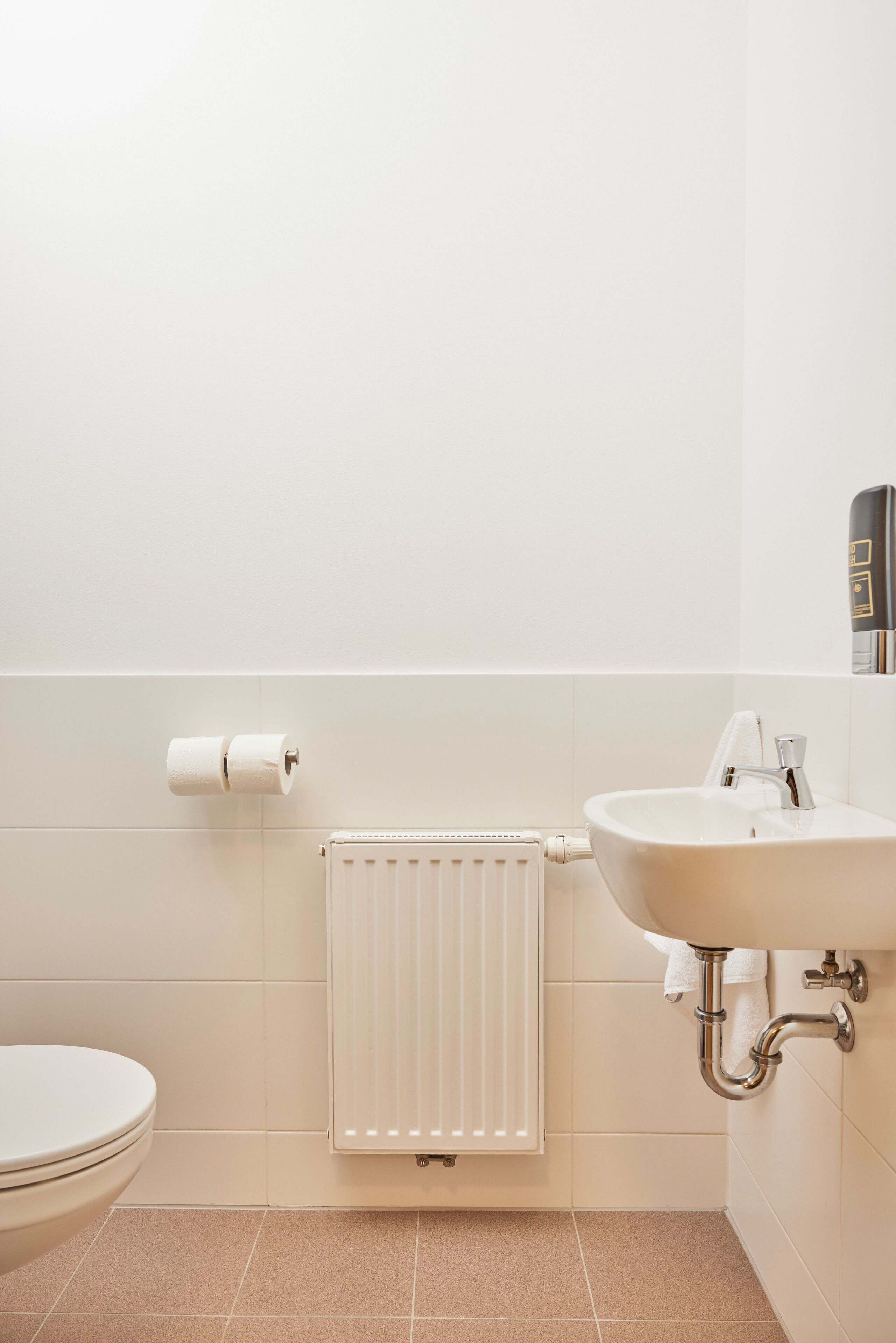 Uma casa de banho com sanita, lavatório branco, toalha e suporte para papel higiénico.