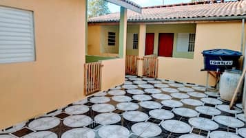 Um pátio com piso de azulejos, um barril azul identificado com 'FORTLEV' e uma antena parabólica no telhado.