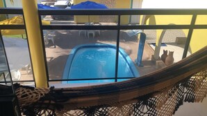 Vista de uma área de piscina com uma rede, uma parede amarela e um guarda-sol azul.