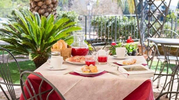 Uma área de refeições ao ar livre com uma mesa posta para o café da manhã, incluindo croissants, um jarro de suco vermelho e uma xícara de café.