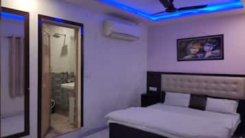 Quarto com cama, ventoinha no teto, ar condicionado e banheiro visível por uma porta de vidro.