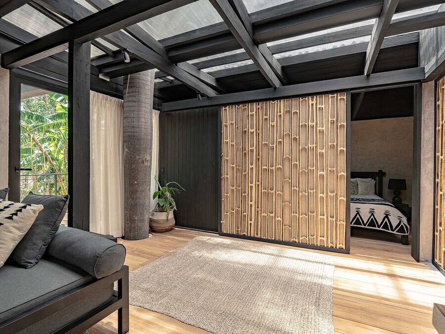 Um interior moderno com um sofá, um pilar imponente, piso de madeira e uma porta deslizante que dá para um quarto.