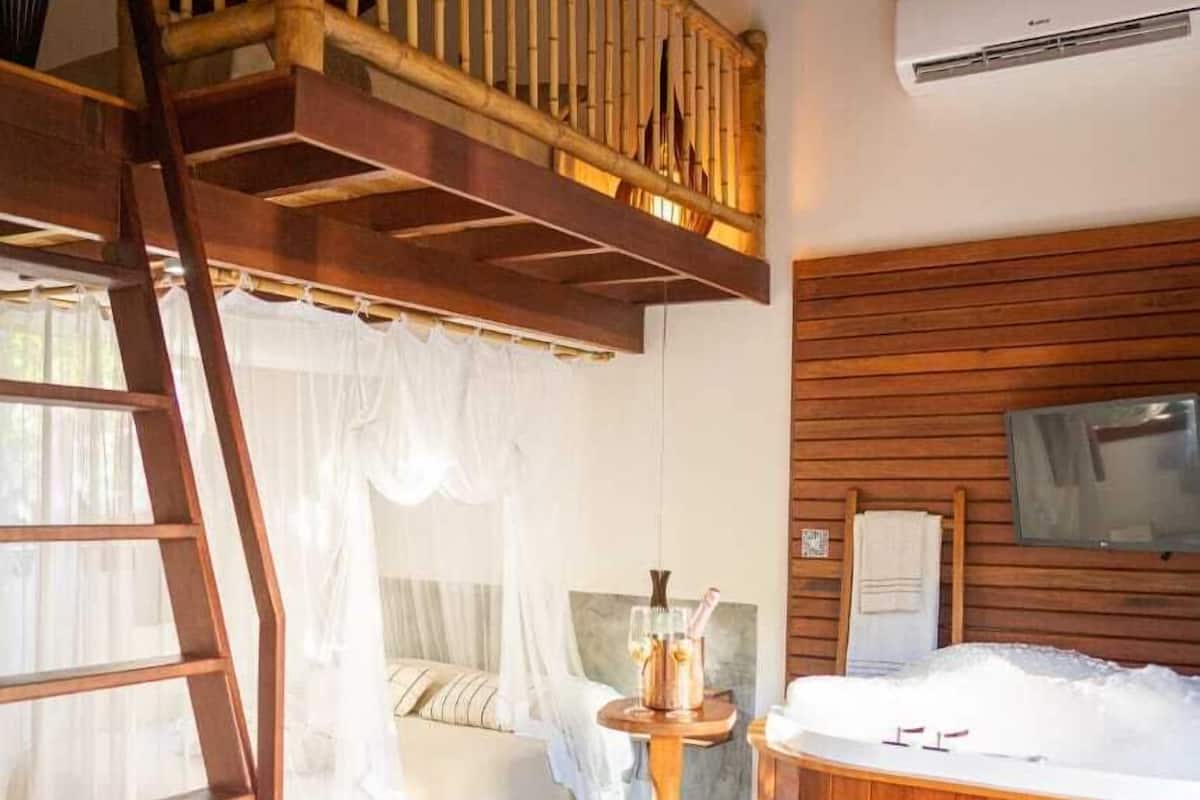 Quarto aconchegante com uma cama beliche de madeira, uma mesa pequena com itens de café da manhã, uma banheira de hidromassagem e uma TV fixada na parede.