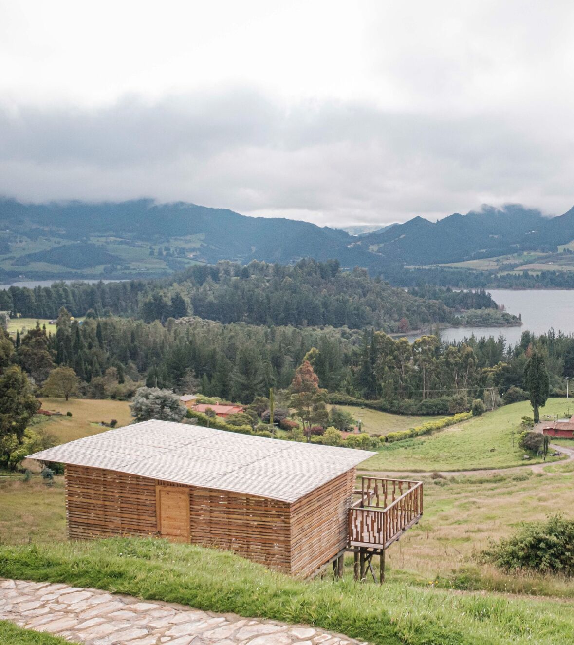 Uma cabana de madeira com varanda, rodeada por uma paisagem exuberante e um lago.