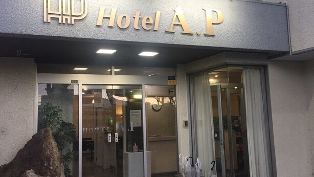 Exterior do Hotel A.P com fachada moderna, entrada de vidro e uma pequena formação rochosa ao primeiro plano.