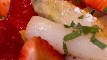 Close-up de salada de frutas com morangos e um vegetal branco, decorada com ervas picadas.