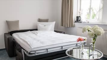 Quarto de hotel com cama, mesa de cabeceira com um vaso de flores e janela com cortinas.