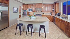 Uma cozinha moderna com armários de madeira, eletrodomésticos de aço inoxidável, uma ilha de granito com banquetas e iluminação pendente.