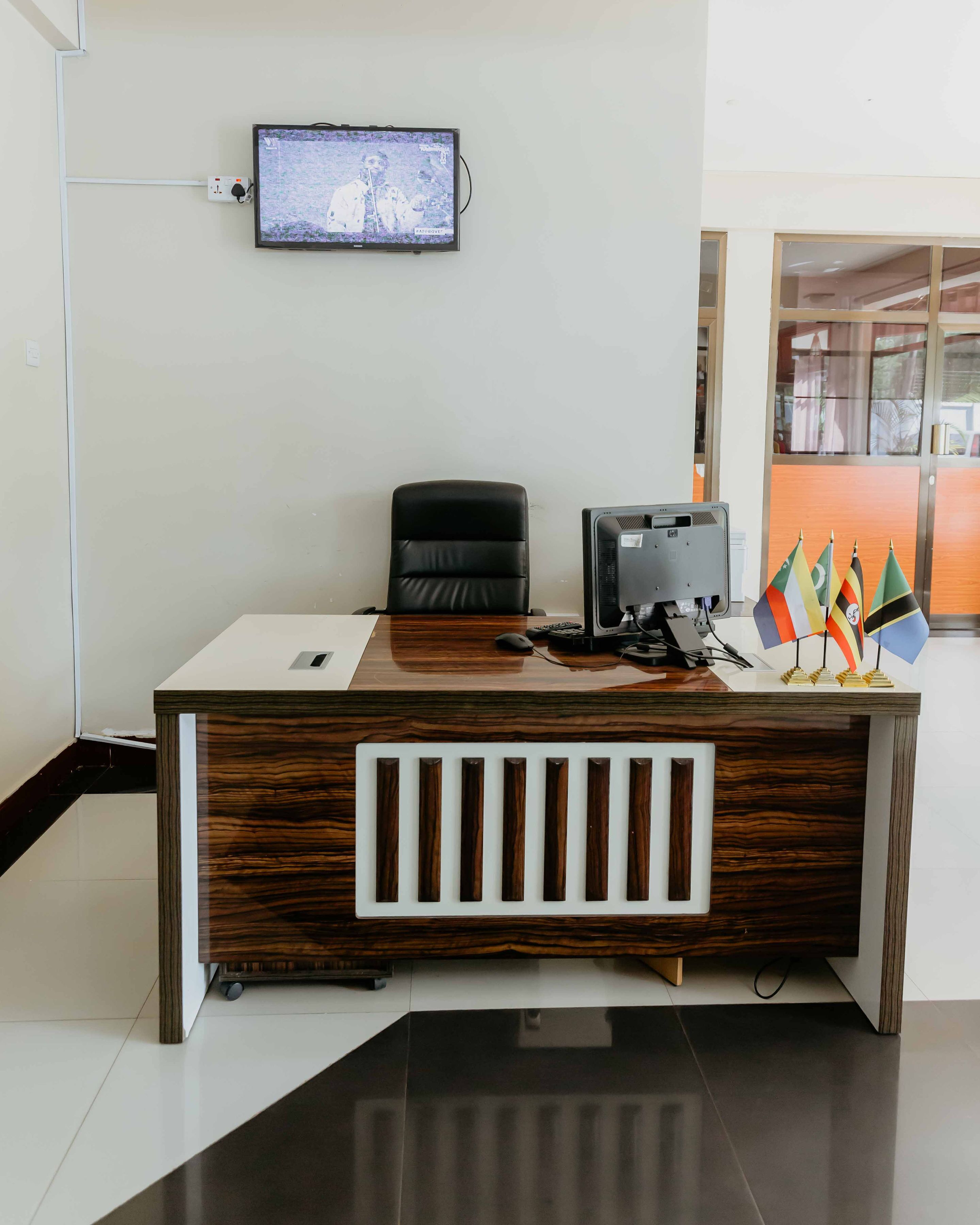 Bancada de recepção com monitor de computador, uma cadeira e exposição de bandeiras.
