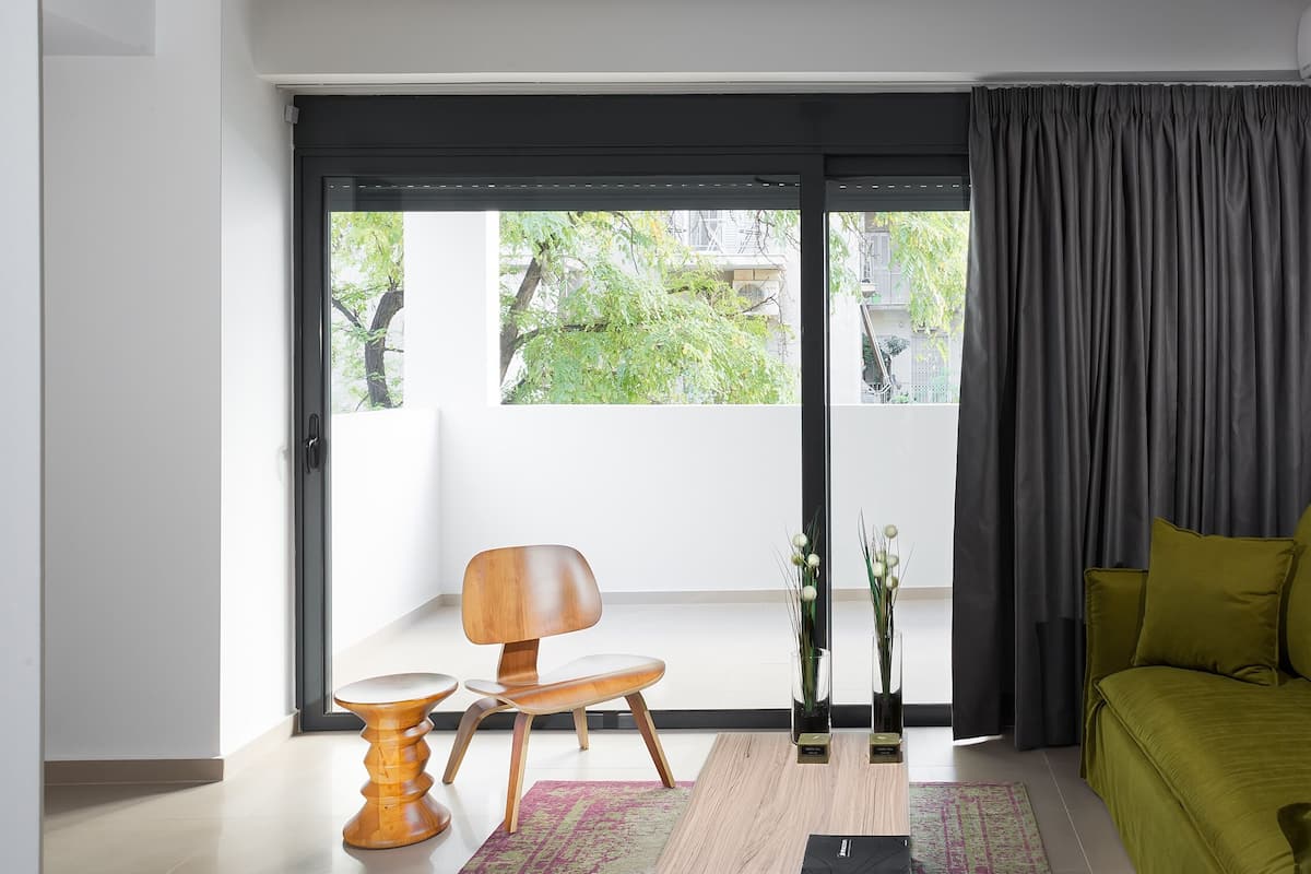 Uma sala de estar moderna com um sofá verde, uma cadeira de madeira, uma mesinha e vista através de uma porta de correr.