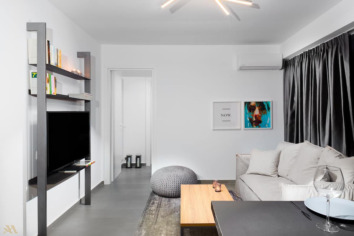 Uma sala de estar moderna com uma TV de tela plana, um sofá, uma mesa de centro e uma estante de livros.