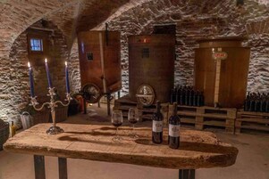 Uma adega rústica com barris de madeira, um candelabro e garrafas de vinho sobre uma mesa.