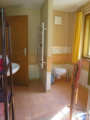 Casa de banho com porta de madeira, lavatório branco, sanita e zona de duche com cortina amarela.
