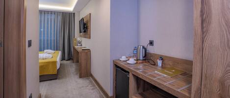 Quarto de hotel com uma cama, escrivaninha com cafeteira e um pequeno frigorífico.