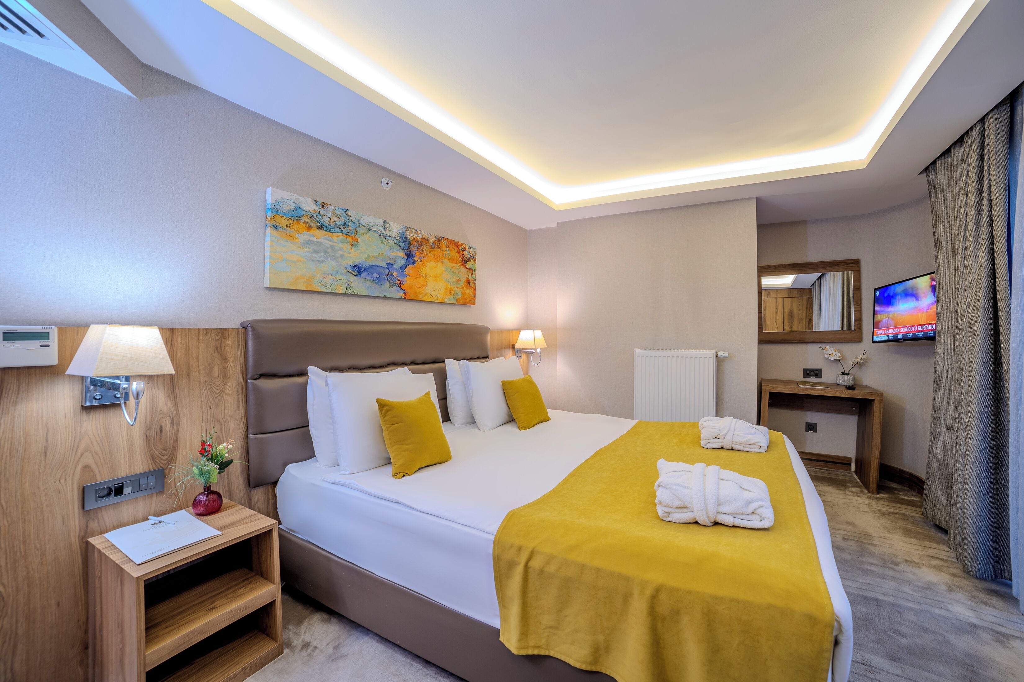 Quarto de hotel com cama, mesa de cabeceira, luminária, obra de arte e televisão.