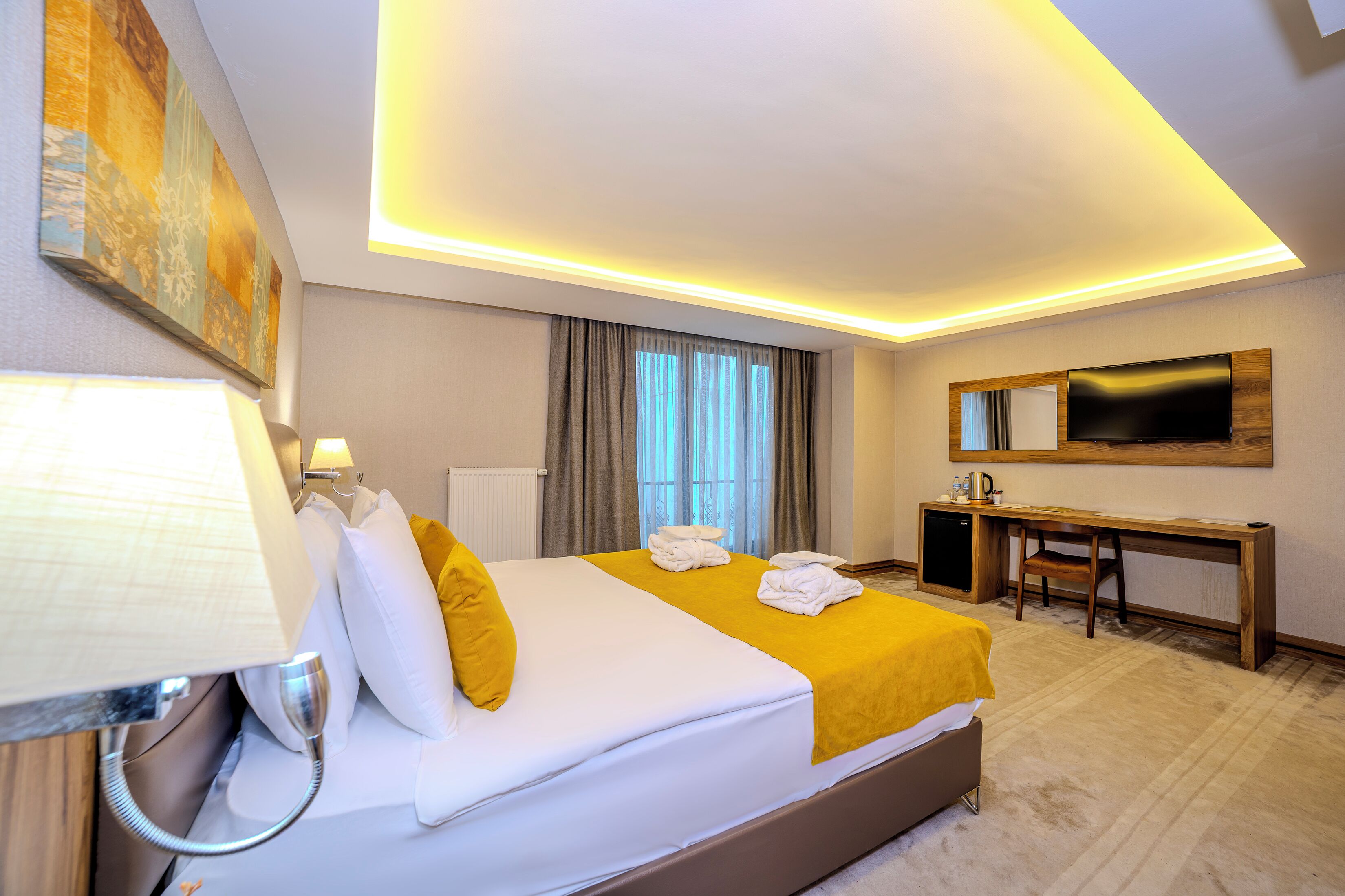 Quarto de hotel com cama, escrivaninha, cadeira, televisão e janela com cortinas.