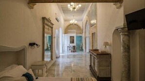 Quarto de hotel com uma cama grande, uma mesinha de cabeceira de madeira, televisão e vista para o corredor.