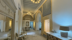 Um hall de hotel espaçoso com teto alto, lustres, piso de mármore e área de estar central com mesas e cadeiras.