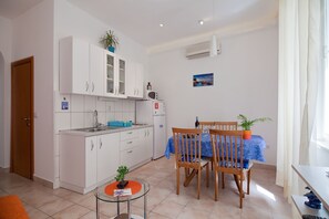 Um espaço compacto com cozinha compacta, área de refeições com duas cadeiras de madeira, uma mesa redonda pequena e um vaso com planta.