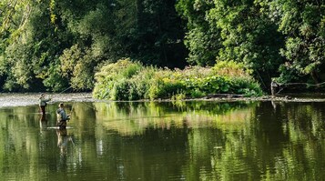 Um rio calmo com duas pessoas pescando, cercado por vegetação densa.