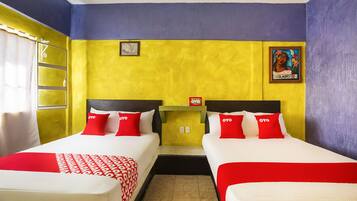 Quarto de hotel com duas camas, cada uma com roupa de cama vermelha e branca, uma escrivaninha pequena com abajur e um quadro na parede.