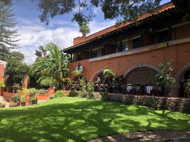 Um pátio com gramado bem cuidado, plantas em vasos e um edifício com telhado de telhas e janelas em arco.