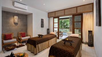 Quarto com duas camas, uma mesa de massagem e um espaço de estar com cadeiras.