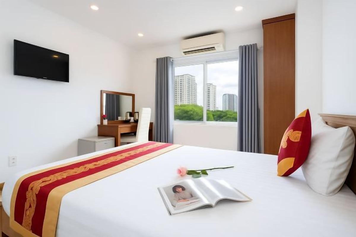 Quarto de hotel com cama, televisão de tela plana na parede, escrivaninha com cadeira, janela com cortinas e aparelho de ar condicionado.