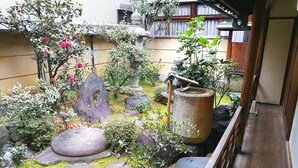 Um jardim japonês tradicional com caminhos de pedra, um espelho d'água e diversas plantas.