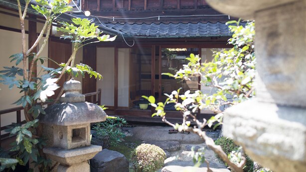Um edifício japonês tradicional com telhado de telhas, lanternas de pedra e um pequeno jardim com pedras e plantas.