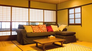 Um quarto japonês tradicional com tatames, uma mesa de madeira baixa e um sofá com almofadas.