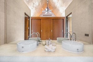 Casa de banho moderna com duas pias grandes, ventoinha no teto e armários de madeira.
