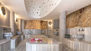 Uma área de spa luxuosa, com piso de mármore, paredes de pedra e grandes vasos decorativos.