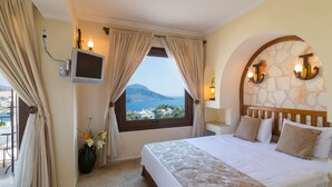 Quarto de hotel com cama, televisão, parede de pedra e vista para o mar.