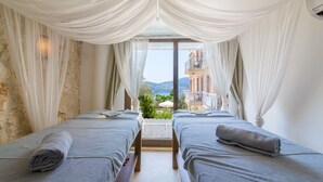 Quarto com duas camas, cortinas leves e vista para um edifício e áreas verdes.