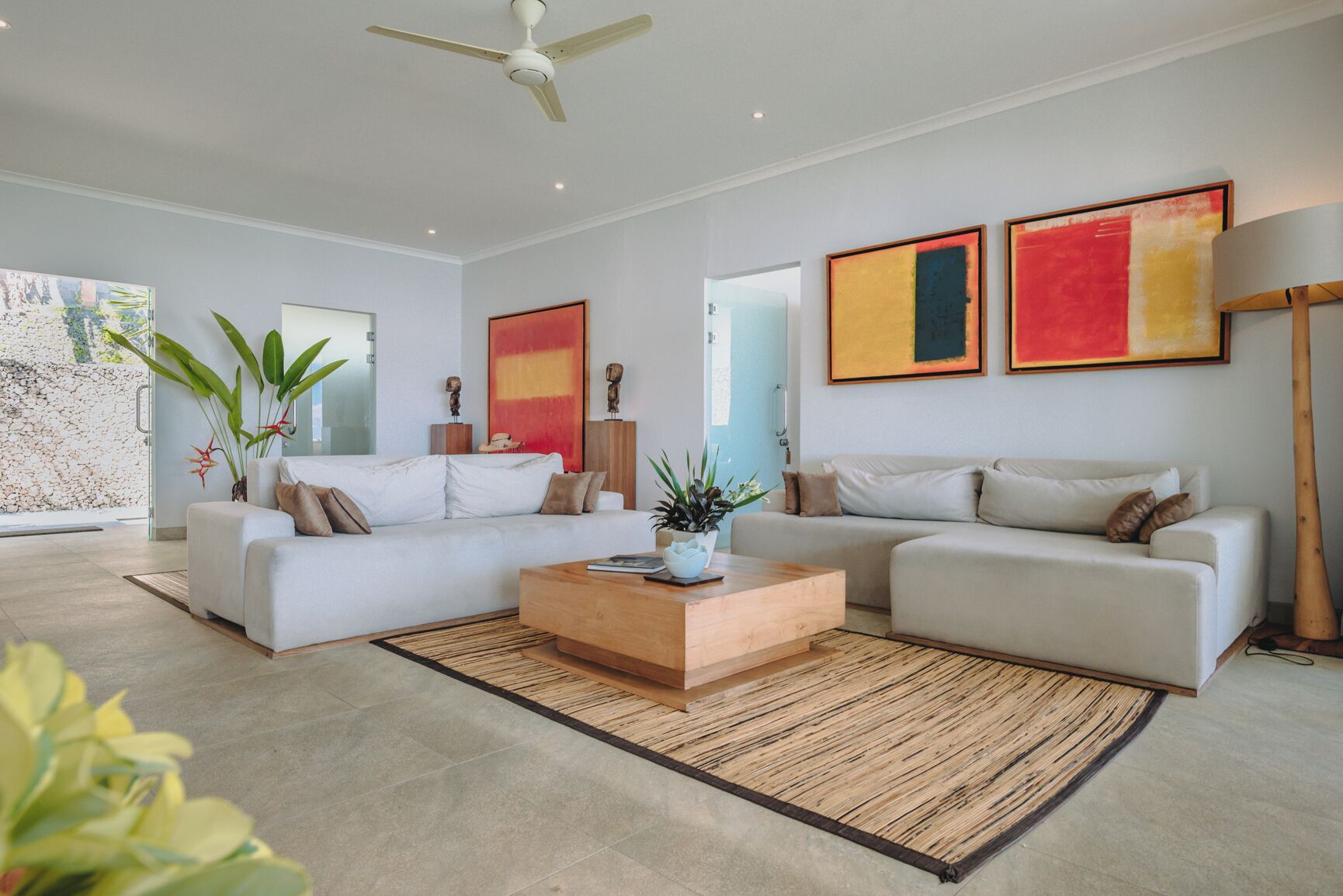 Uma sala de estar moderna com dois sofás brancos, uma mesa de centro de madeira e quadros abstratos nas paredes.