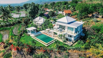 Uma casa moderna de dois andares com piscina, cercada por vegetação exuberante e palmeiras.