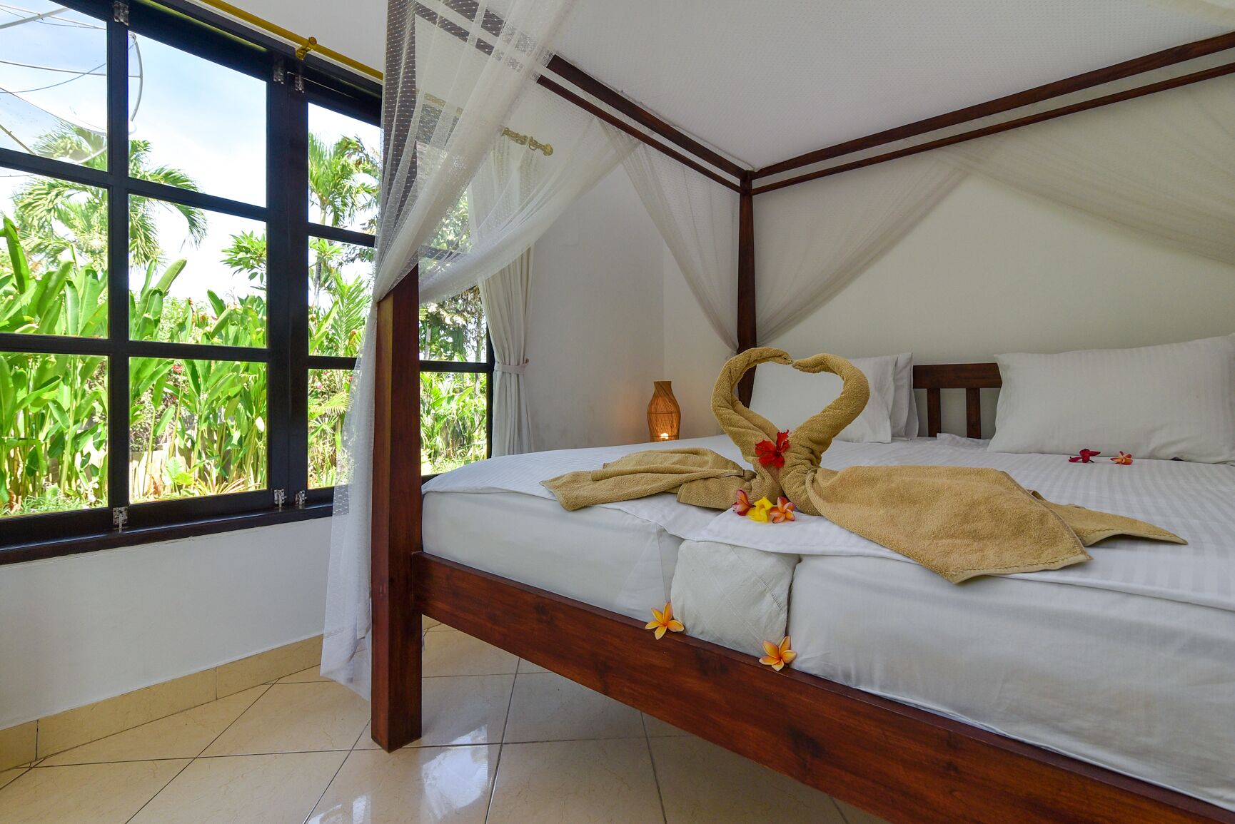 Uma cama com dossel, roupa de cama branca e arranjo de toalhas em formato de coração.