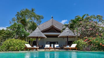 Um resort com piscina, espreguiçadeiras e estruturas com telhado de palha.