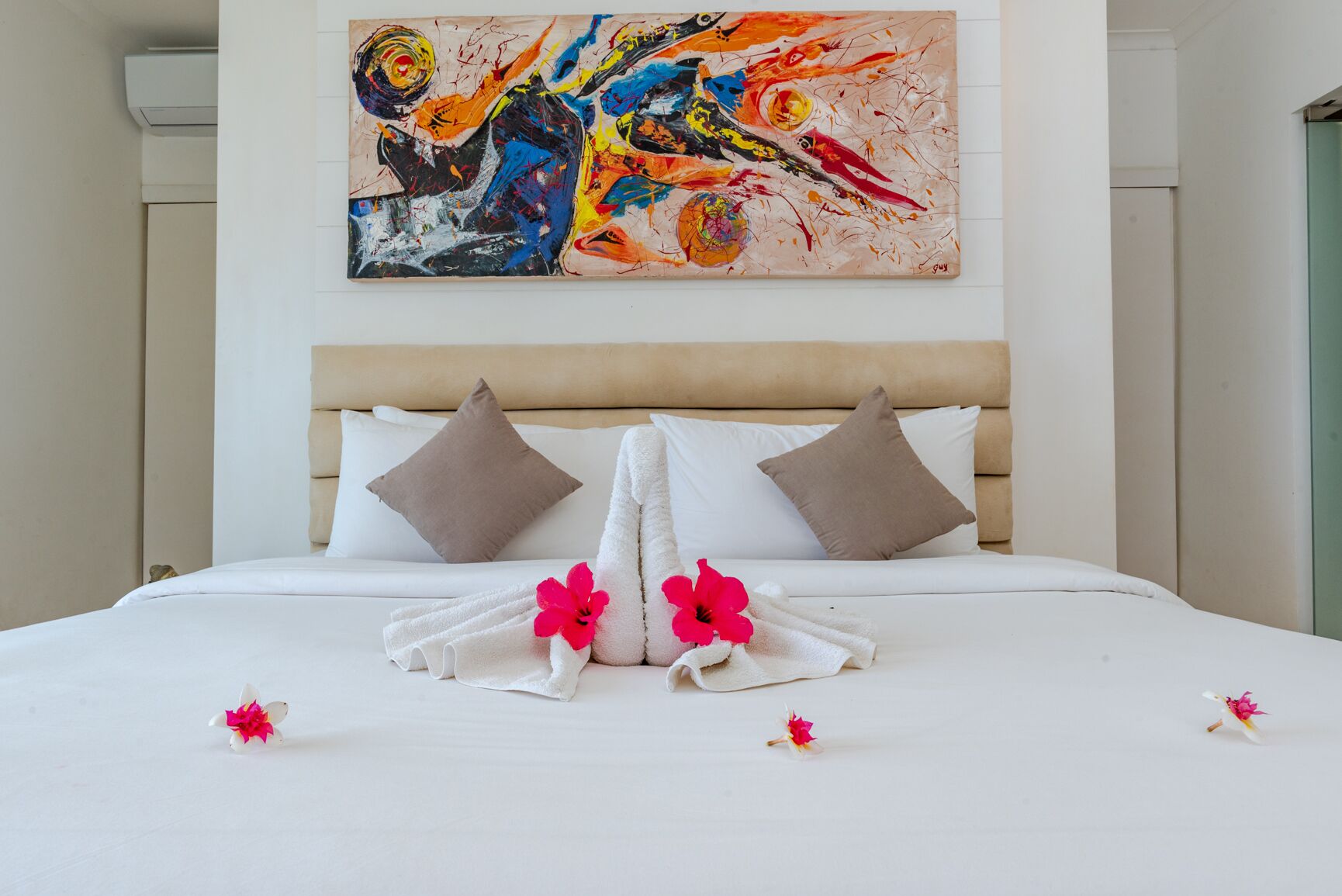 Cama bem arrumada com lençóis brancos, duas almofadas e um arranjo floral.
