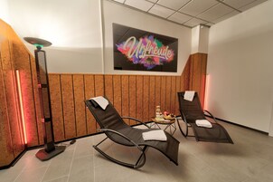 Uma sala de spa com duas cadeiras reclináveis, uma mesa de massagem, uma cadeira de massagem e um aparelho de massagem fixado na parede.
