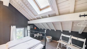 Quarto com cama, janela, ventilador de teto, cadeira e mesa pequena.