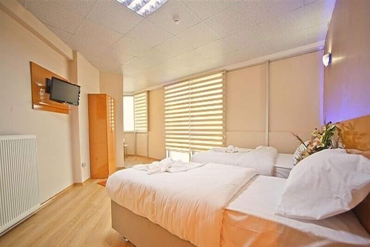Quarto moderno com uma cama grande, televisão presa na parede e janela com persianas.