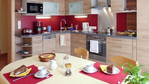 Uma cozinha moderna com armários de madeira, micro-ondas, cafeteira e mesa de jantar posta com bolo e chá.