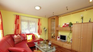 Uma sala de estar com um sofá vermelho, uma mesa de centro de vidro, uma televisão e um armário de madeira.