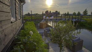 Um deck de madeira com vista para um rio e uma ponte, rodeado por vegetação e um prédio de madeira.