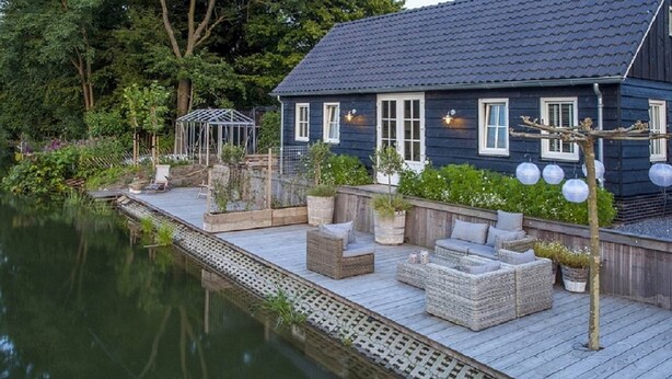 Uma casa com um deck de madeira, móveis de exterior e um jardim.