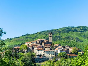 Uma aldeia na encosta com edifícios tradicionais, uma torre imponente e vegetação exuberante.