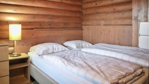 Um quarto estilo cabana de madeira, com uma cama, uma mesinha de cabeceira e uma luminária.