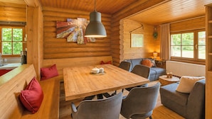 Interior acolhedor de uma cabana, com uma mesa de jantar de madeira, assentos e uma janela grande.